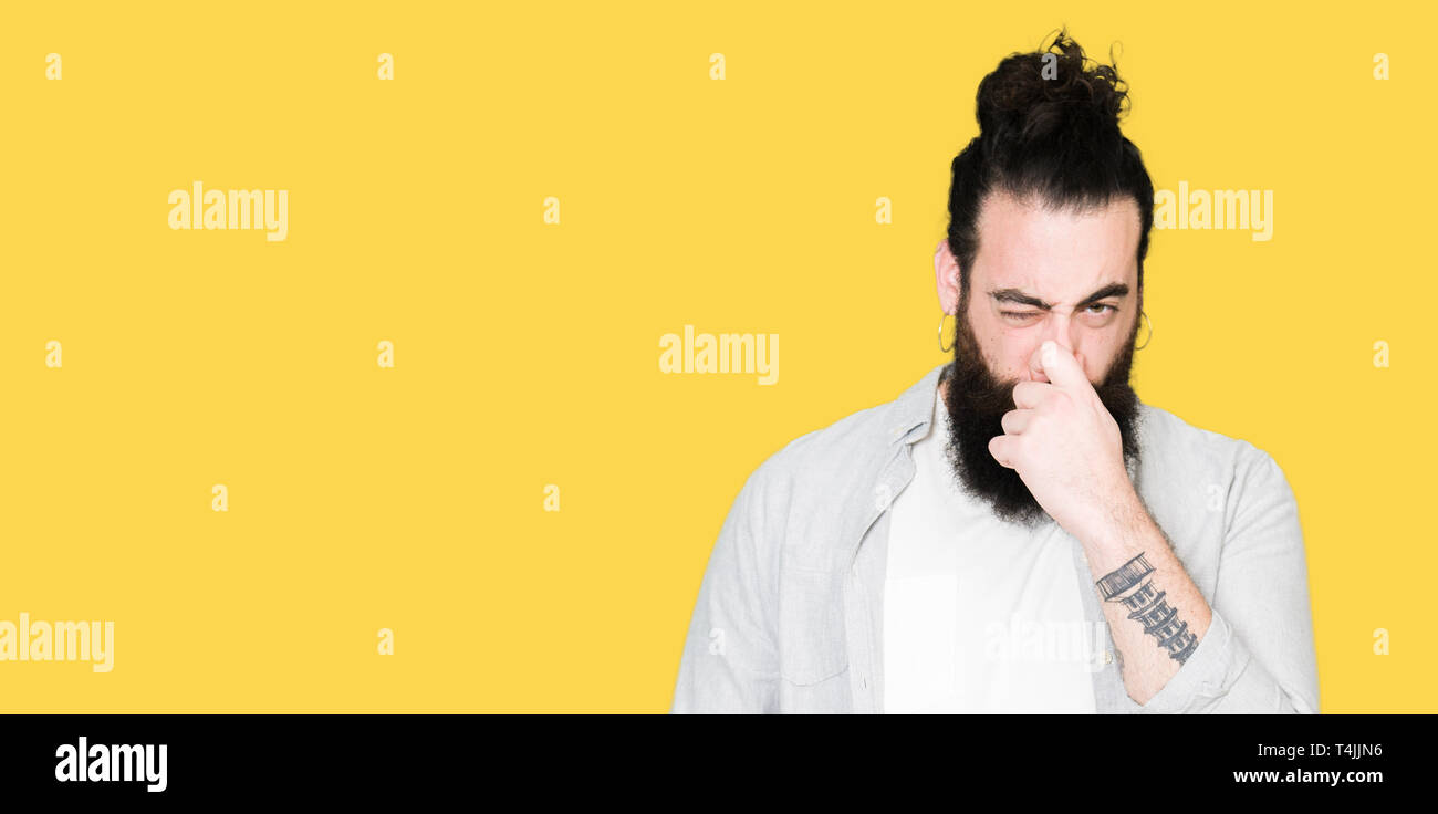 Young man with long hair, beard and earrings smelling something stinky ...
