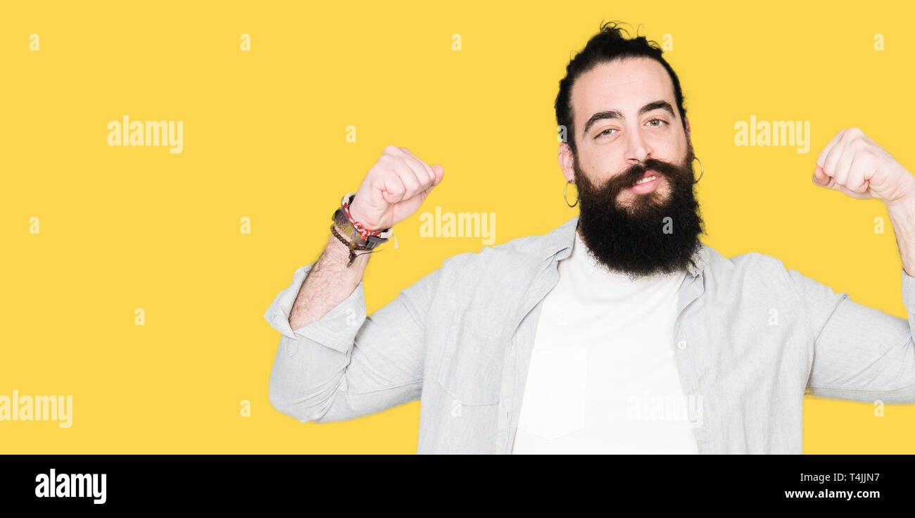 Young man with long hair, beard and earrings showing arms muscles ...