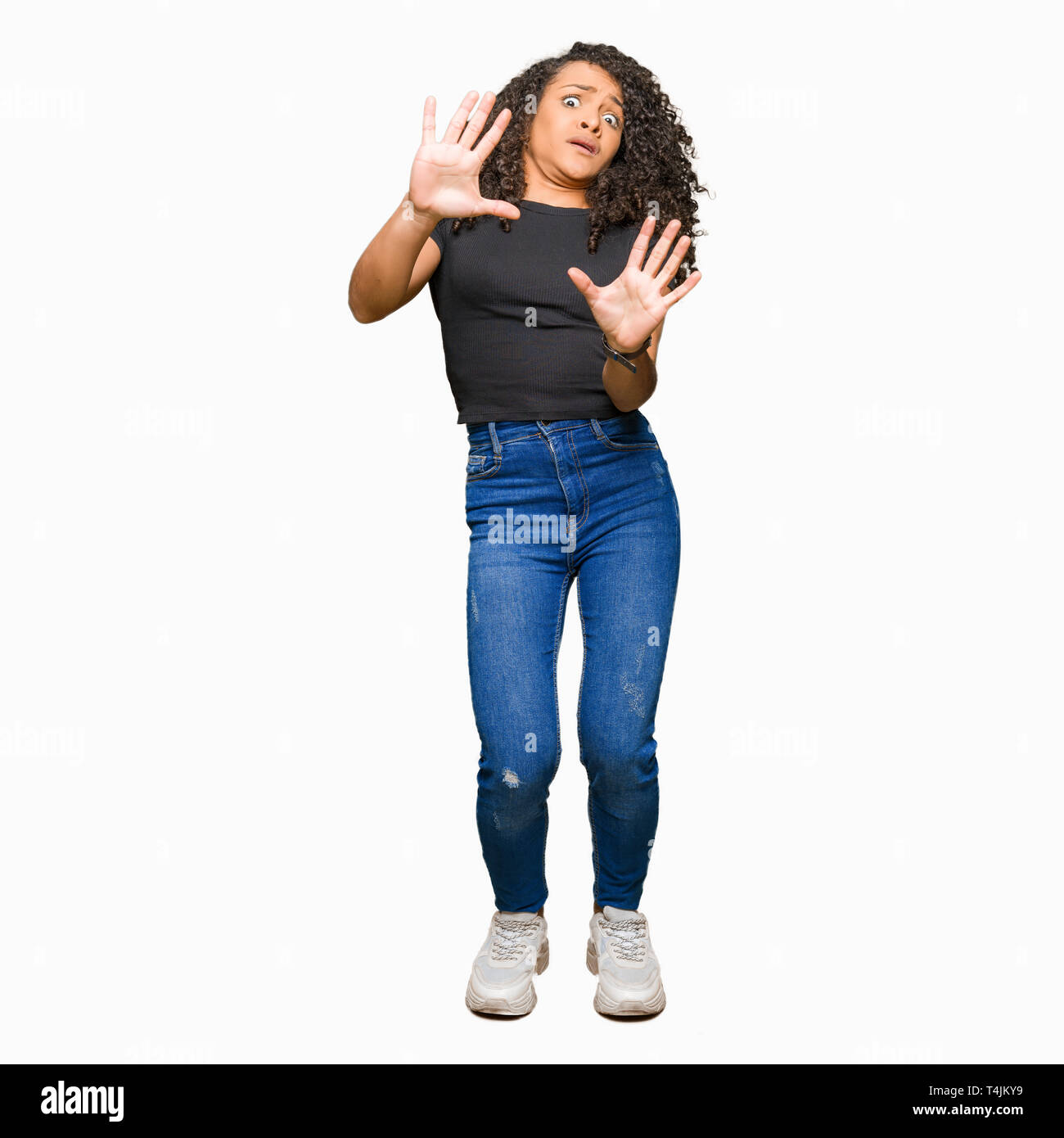 Young beautiful woman with curly hair afraid and terrified with fear ...