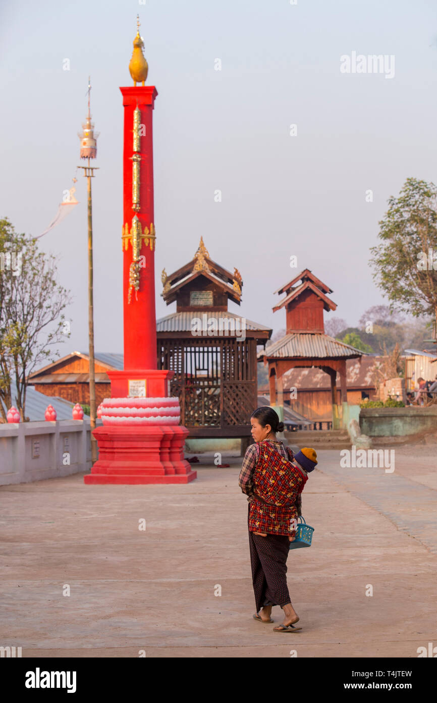 Shan woman carrying her child in a baby carrier across the courtyard of ...