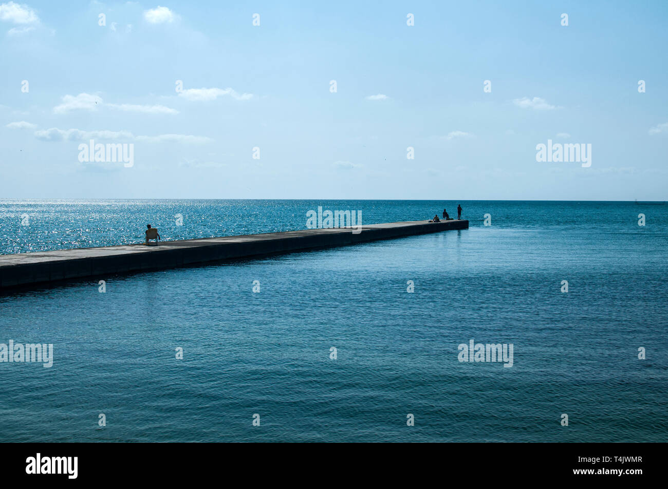 Stone quay in sea bay of calm blue sea waters and three human ...