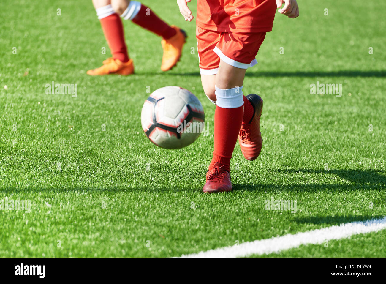 Legs of a soccer player boy in red sports uniform with a ball on a ...