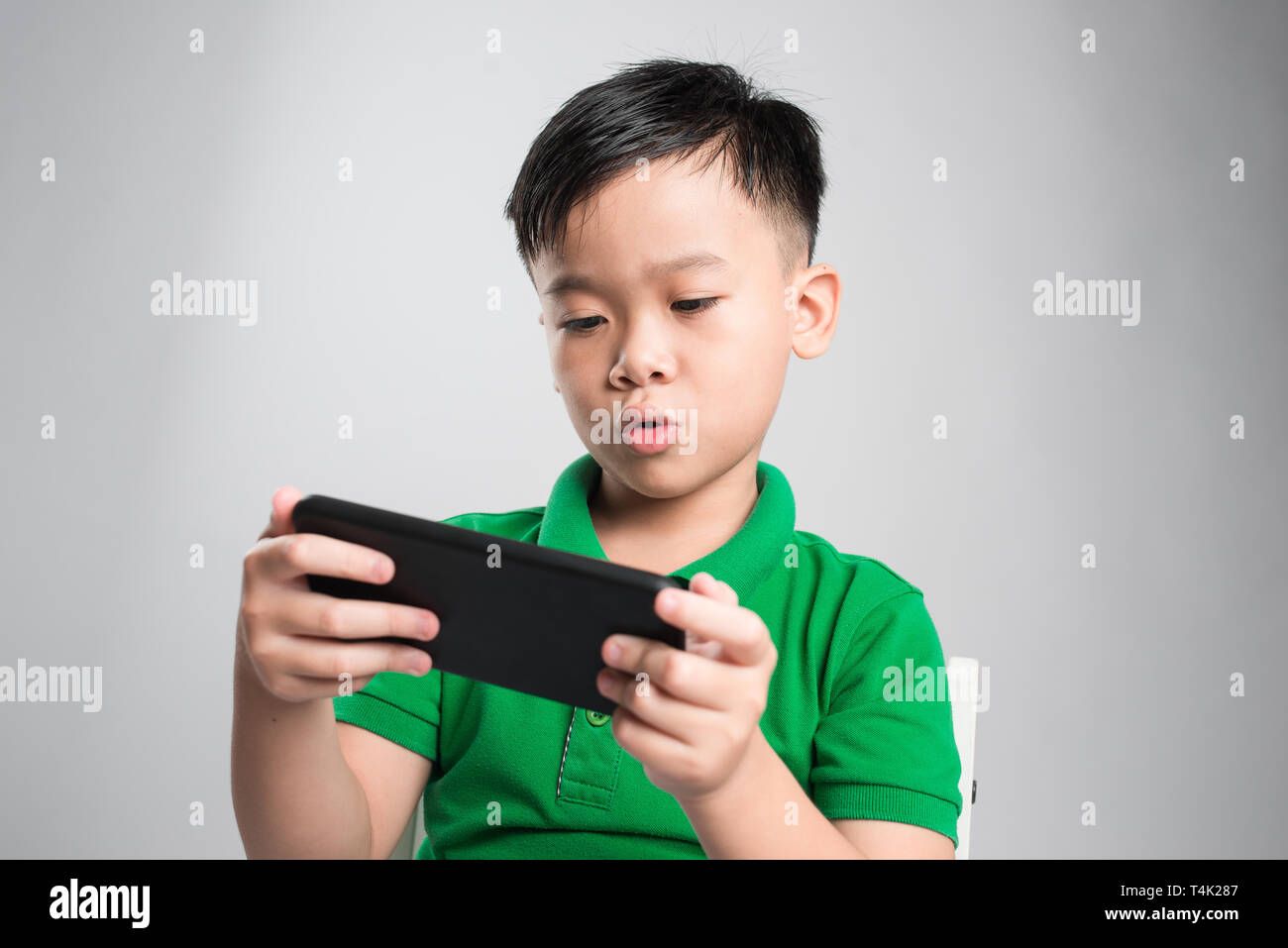 Portrait of an amused cute little kid playing games on smartphone ...