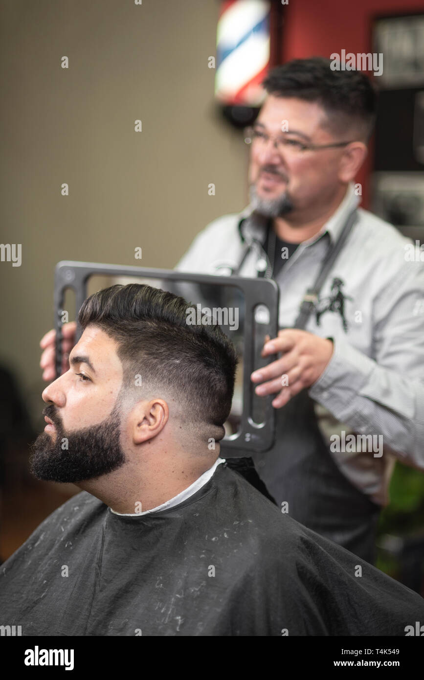 Handsome bearded man looking in the mirror after haircut, at barber ...