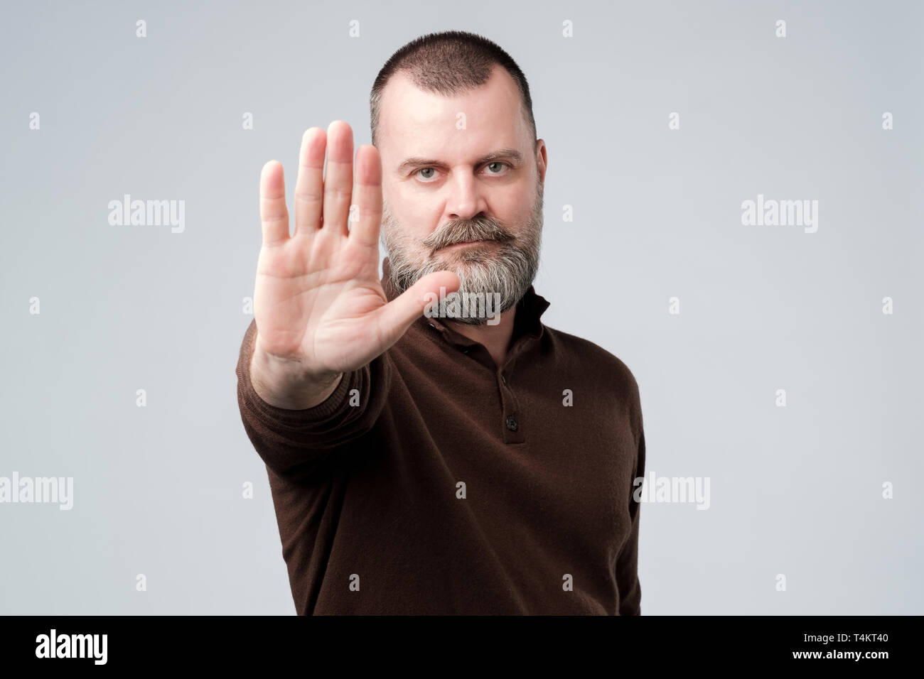 Mature man making stop sign over gray background. Studio shot. I refuse ...