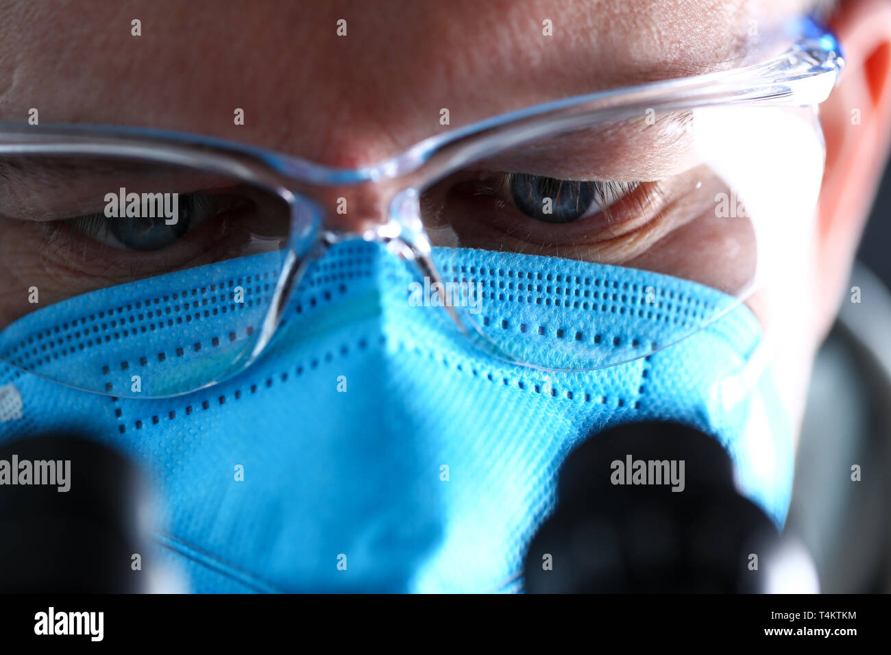Male lab worker eyes looking at microscope wearing protective mask ...