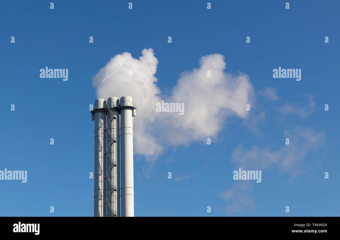 White smoke comes from a white chimney pipe on a background of blue sky ...
