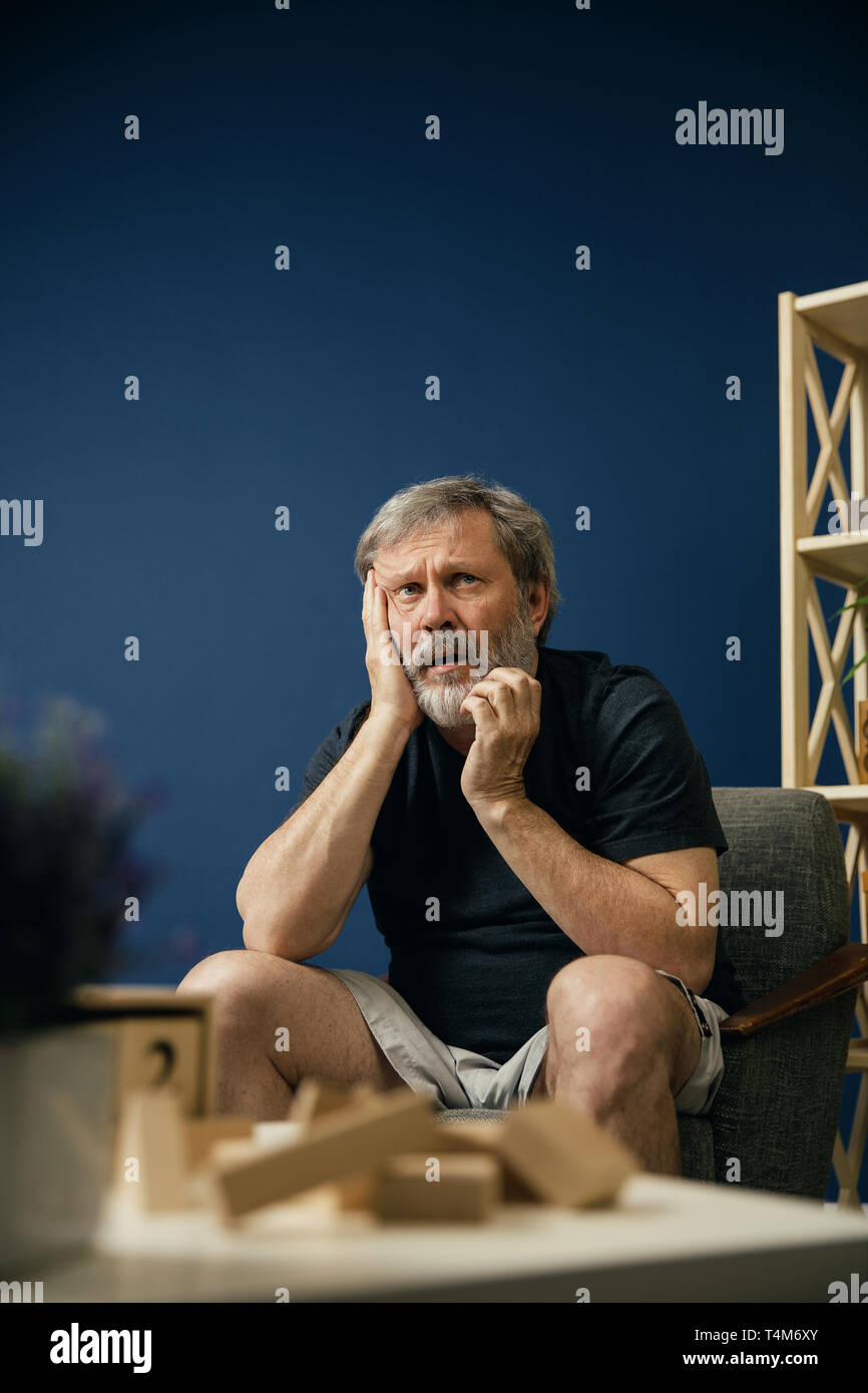 Scared of all around. Old bearded man with alzheimer desease sitting on ...