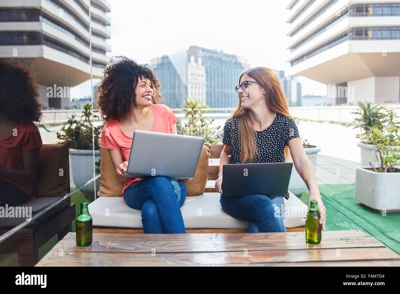Two women as friends with laptop computer relax with beer at the end of ...