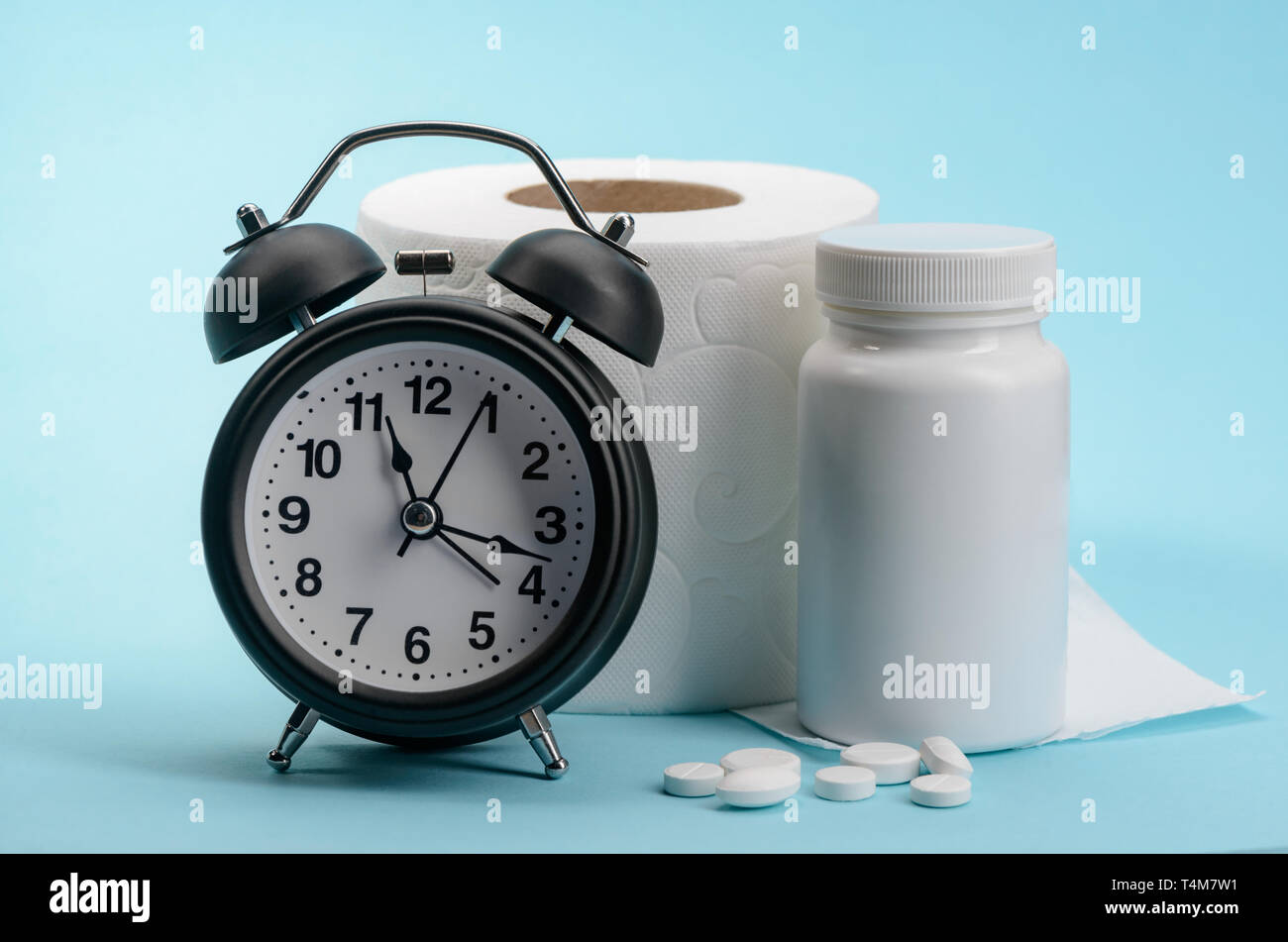 Alarm clock, toilet paper and laxative pills on blue background. Fast ...