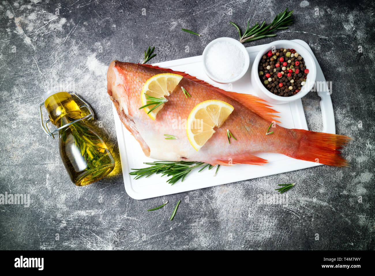 Fish raw snapper with lemon slices, herbs rosemary, salt and pepper on ...