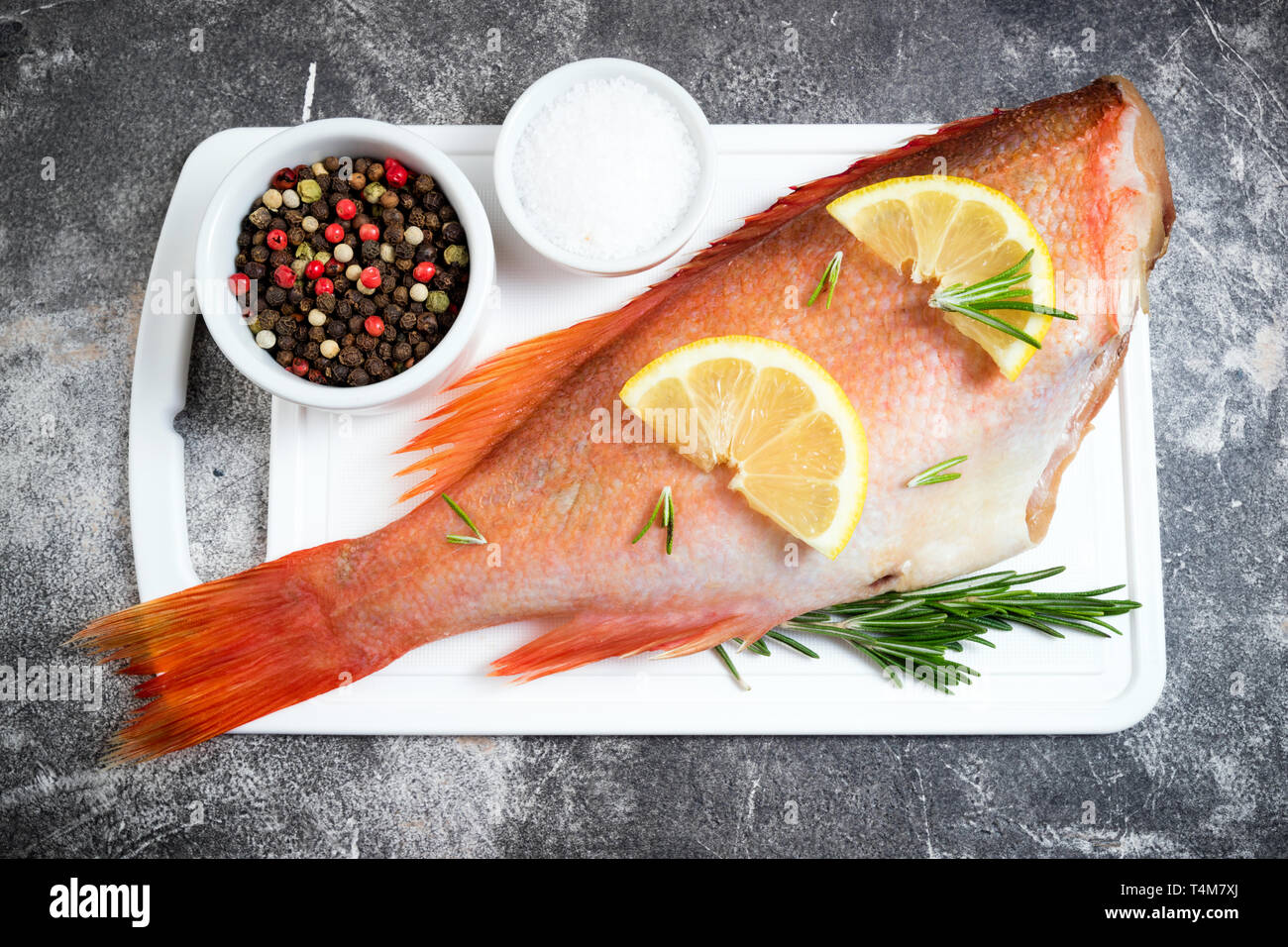 Fish raw snapper with lemon slices, herbs rosemary, salt and pepper on ...