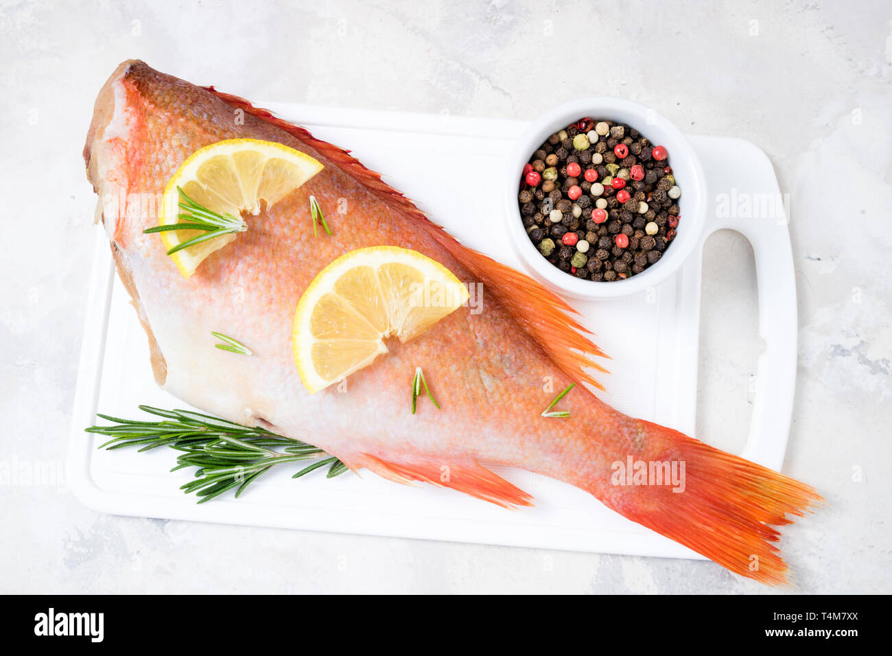 Fish raw snapper with lemon slices, herbs rosemary, salt and pepper on ...