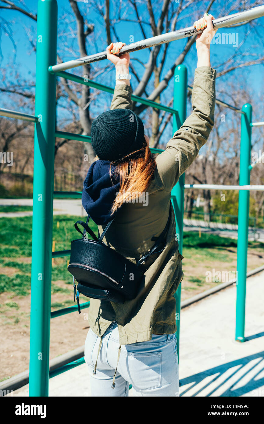 Back view female dressed in casual clothes with backpack doing pull-ups ...
