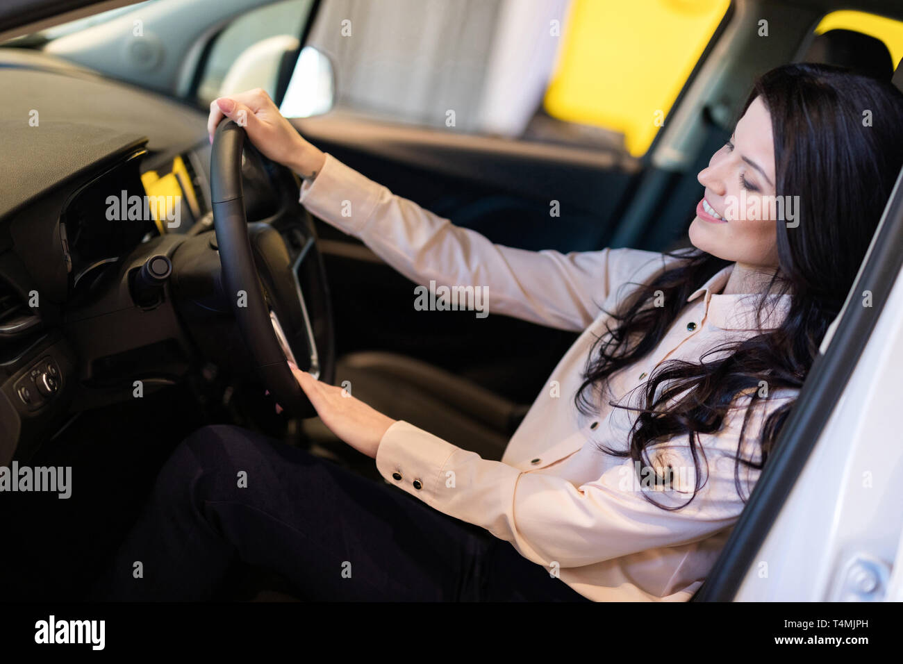 Side view of beautiful happy woman sitting in her new car and examines ...