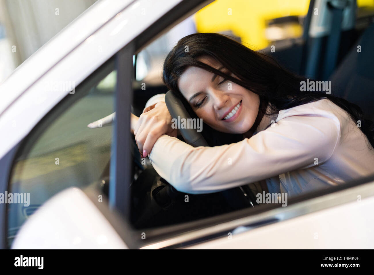 Side view of beautiful happy woman sitting in her new car and examines ...