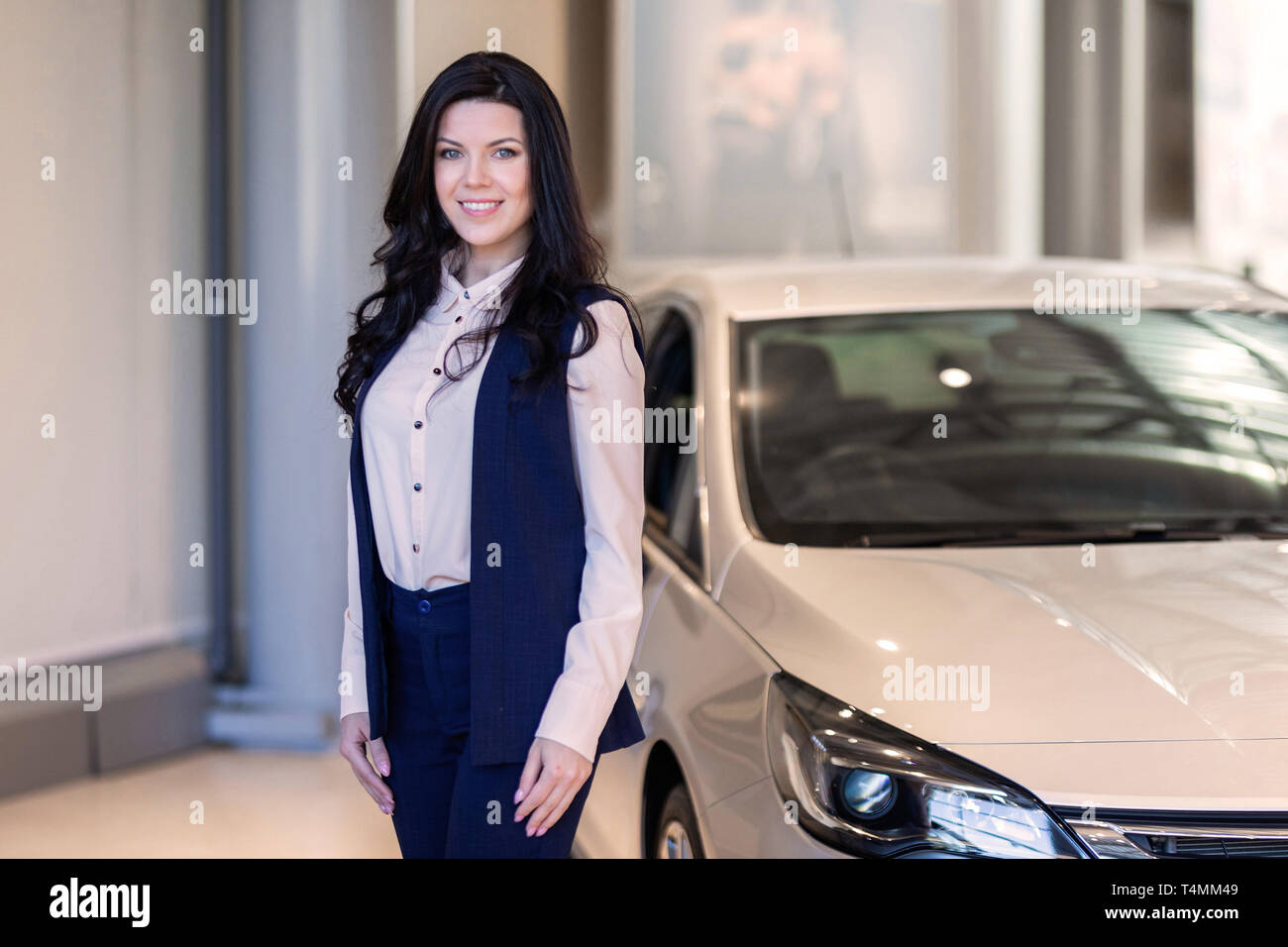 Beautiful woman in dealership center staying near new car. Shows ...
