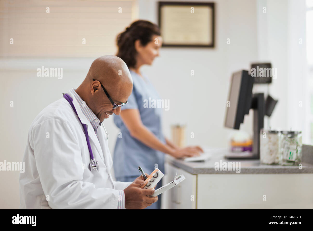 Smiling male doctor taking notes on a clipboard as he holding a box of ...