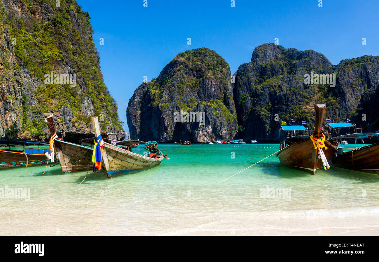 Long-tail boats on a Maya Bay sandy beach, surrounded by tall mountains ...