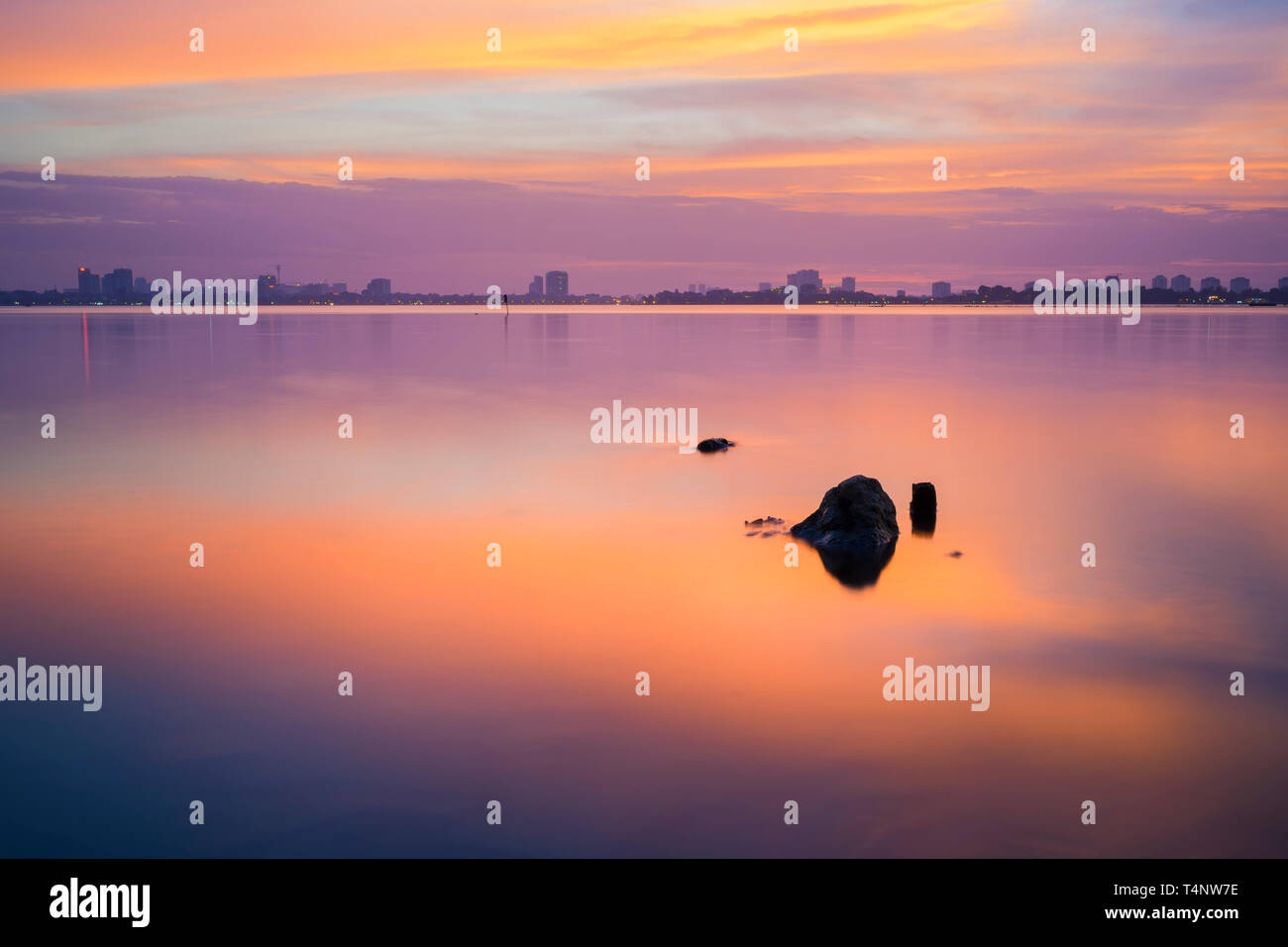Calm lake in sunset with city building on background. Focus on the rock ...