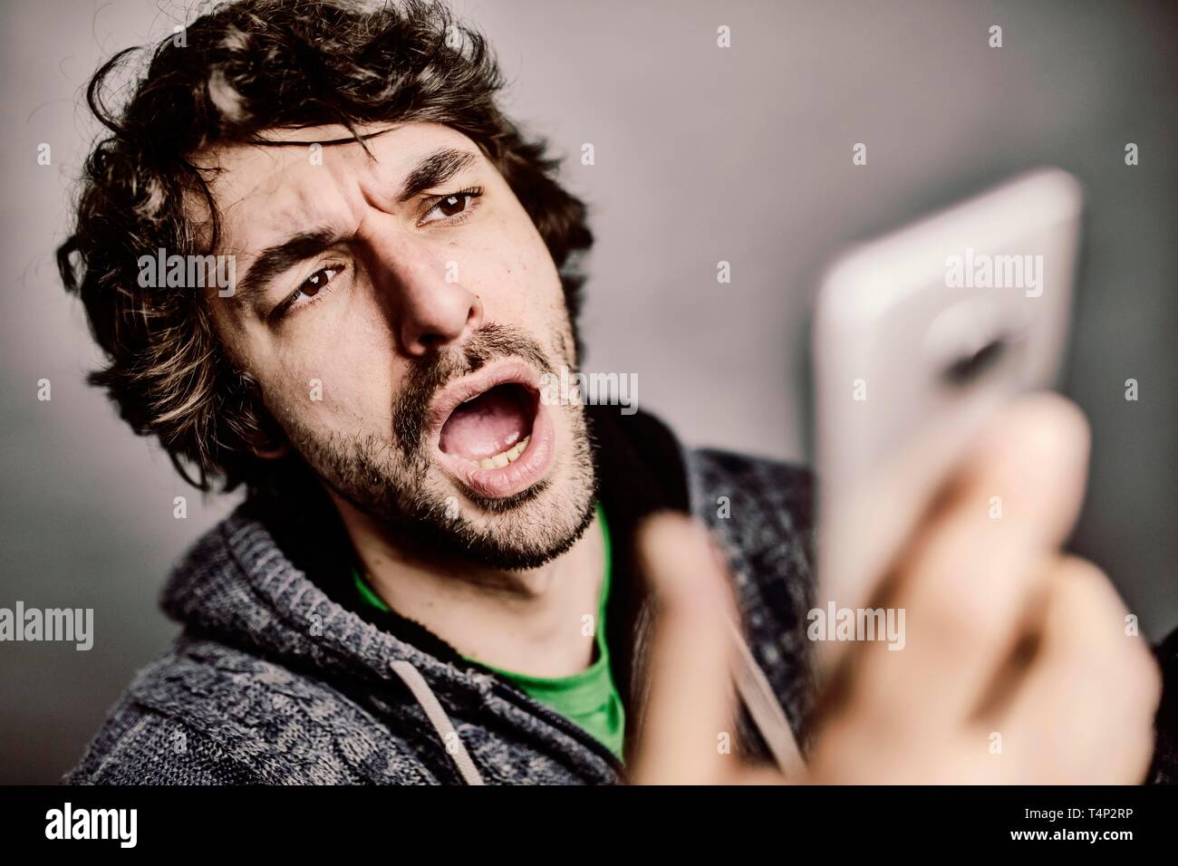 Young man looks angry, angry, surprised at his smartphone, studio shot ...