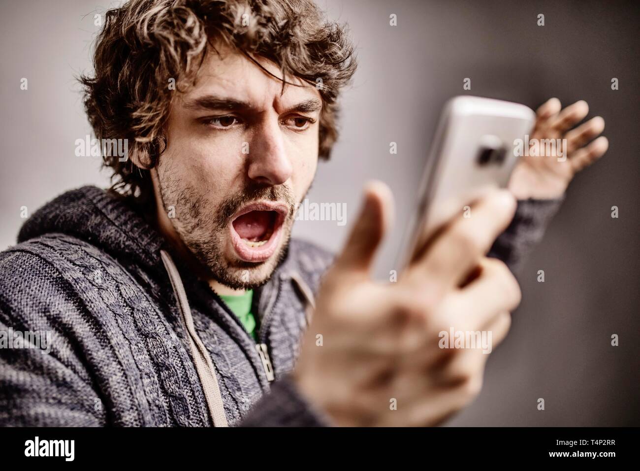 Young man looks angry, angry, surprised at his smartphone, studio shot ...
