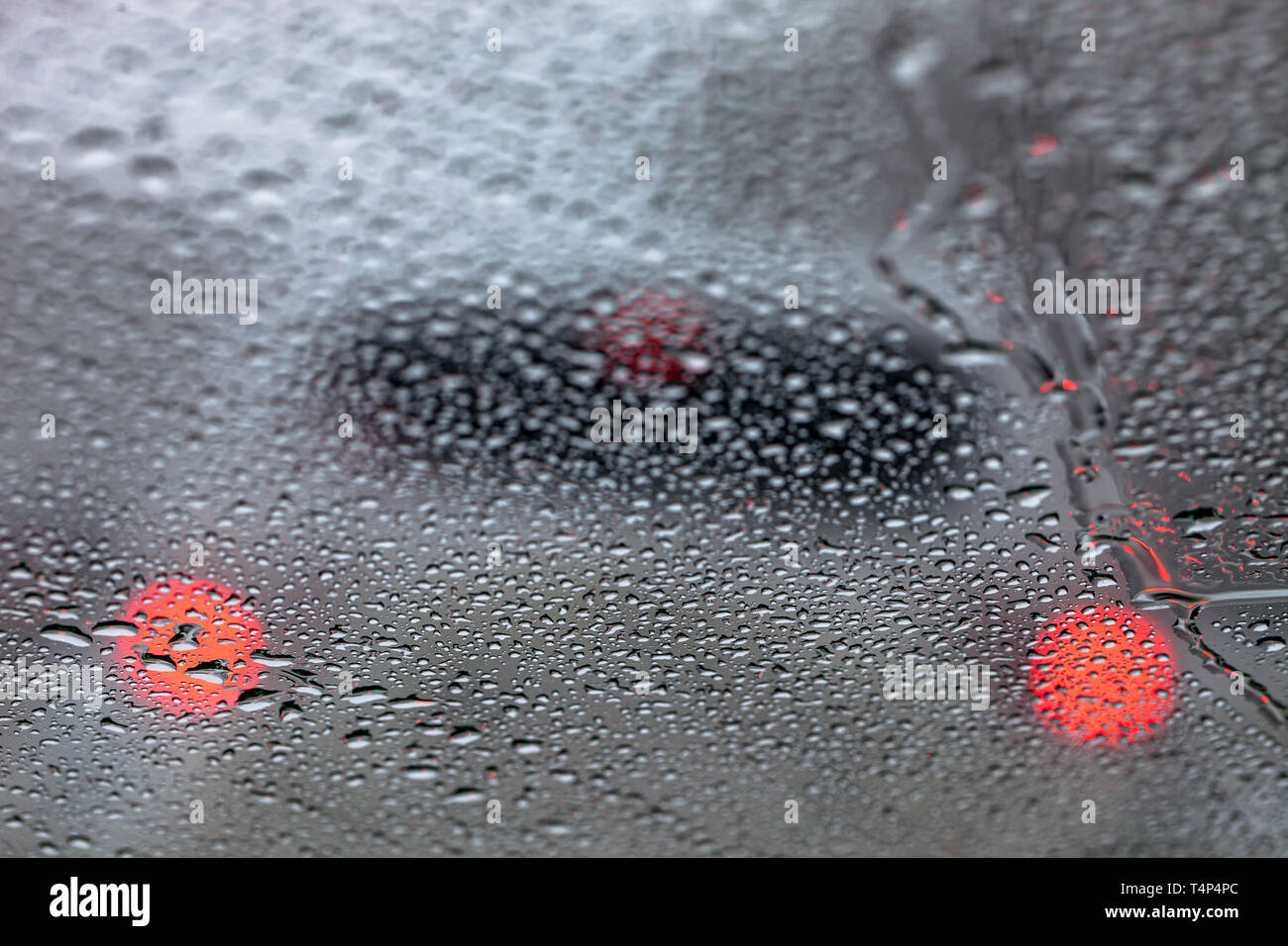 Windshield of the car during heavy rain. A car in front with bright red ...