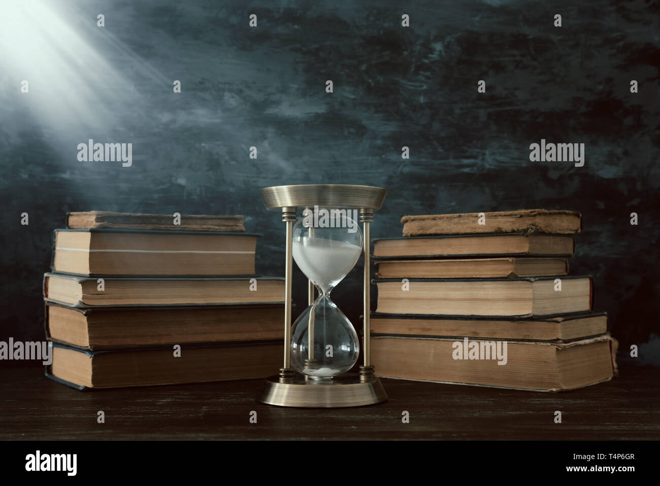 Hourglass as time passing concept and old books in front of black wall ...