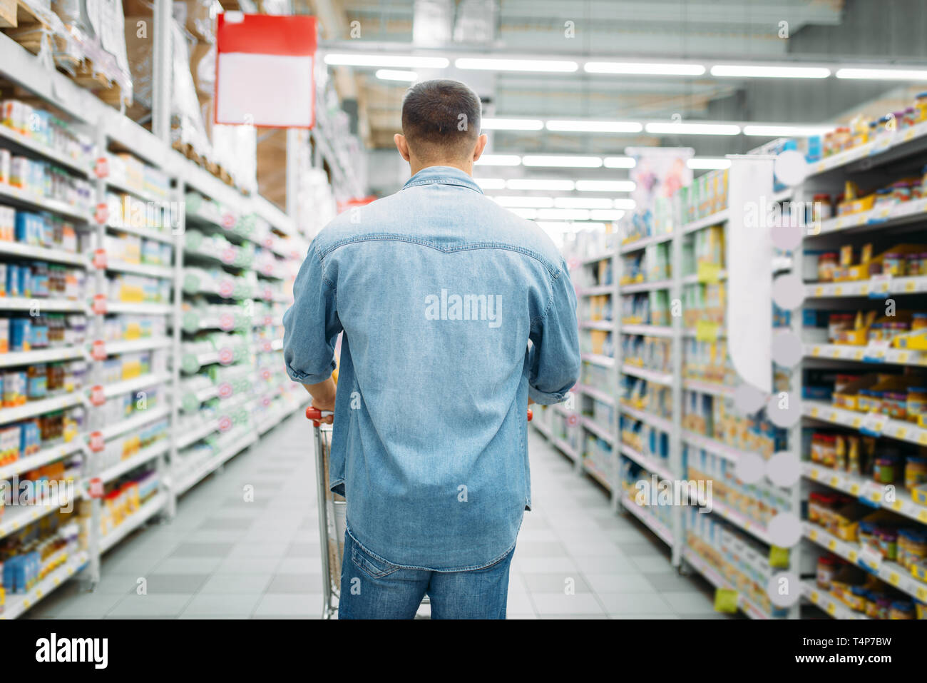 Man with cart makes a purchase in supermarket, back view. Male customer ...