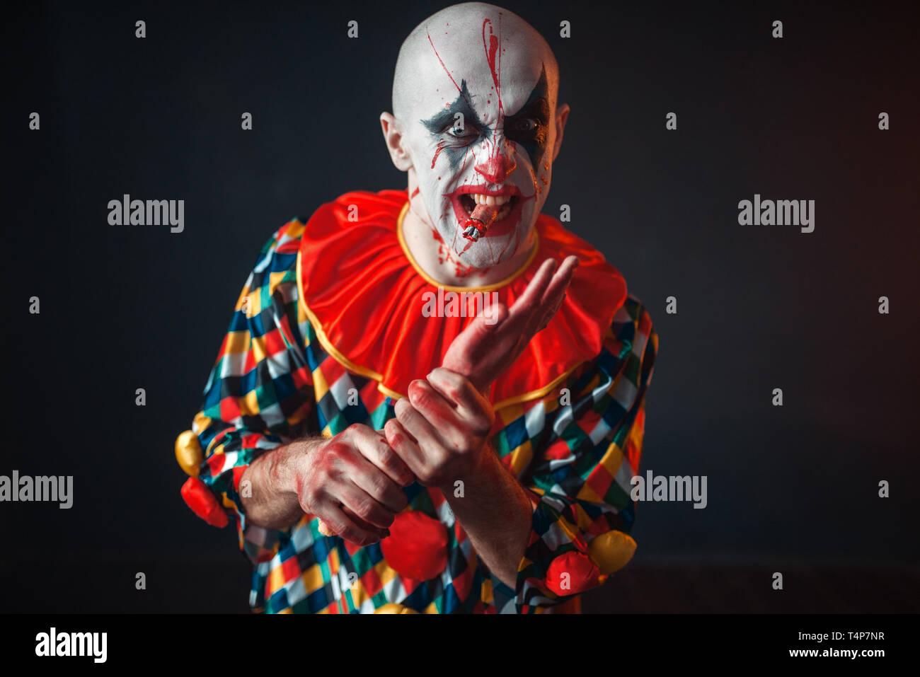 Mad bloody clown holds human hand, finger in his teeth. Man with makeup ...