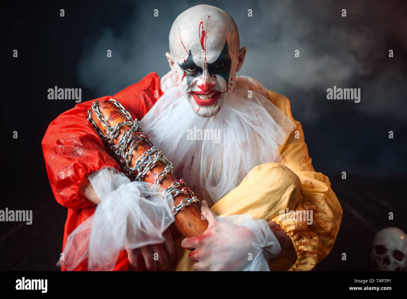 Scary bloody clown with baseball bat sitting on the floor, around the ...