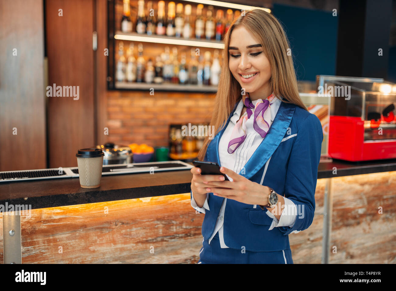 Stewardess using mobile phone in airport cafe. Air hostess in waiting ...