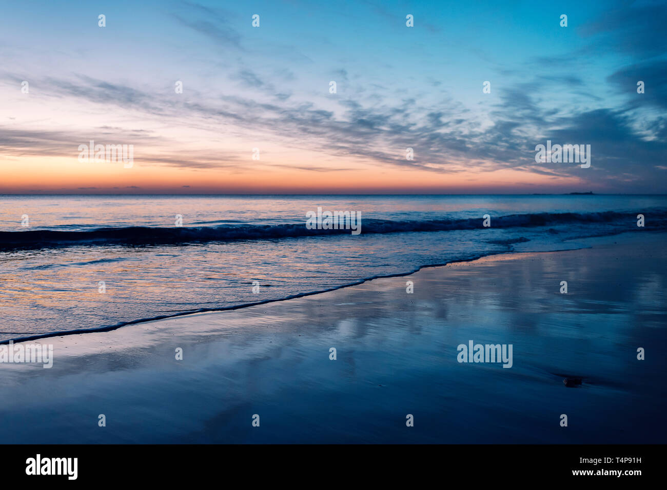 beautiful sunset on a lonely beach, the wet sand of the beach reflects ...