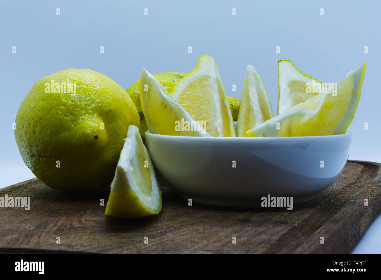 whole lemon and lemon wedges inside a white bowl on a wooden board in ...