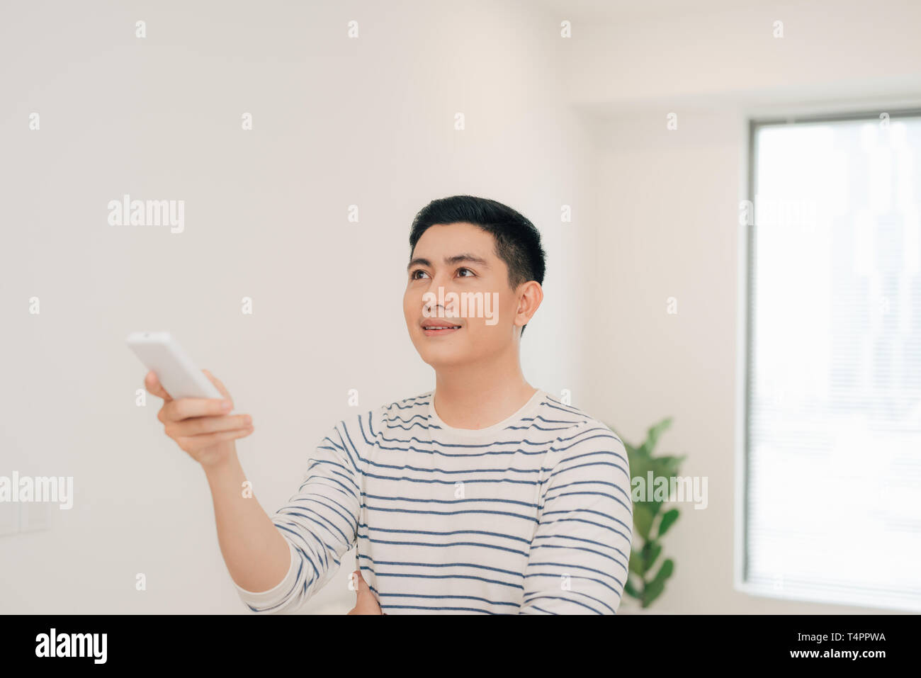 Portrait of happy man using remote control to operate air conditioner ...