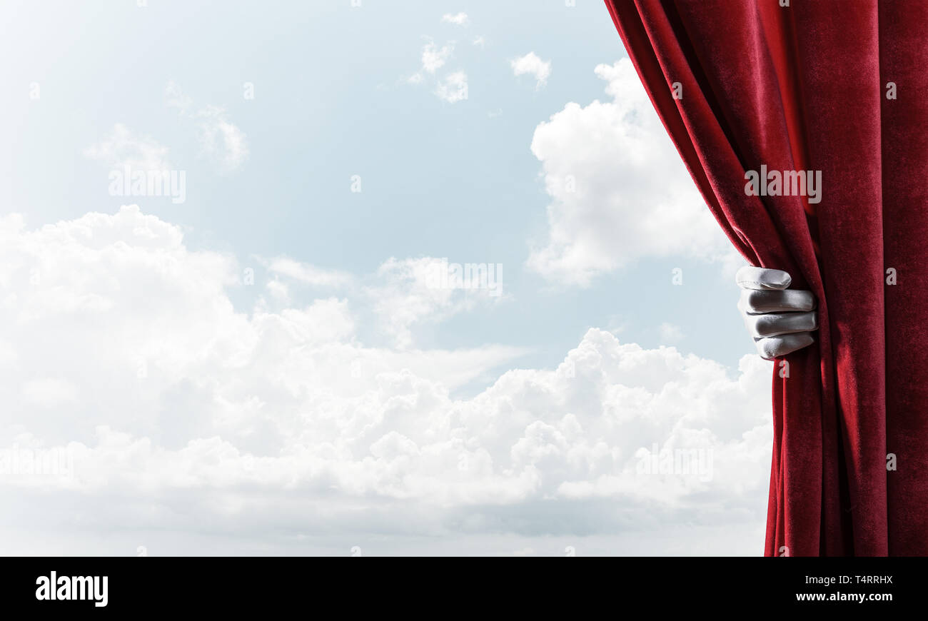 Human hand in glove opens red velvet curtain on blue sky background ...
