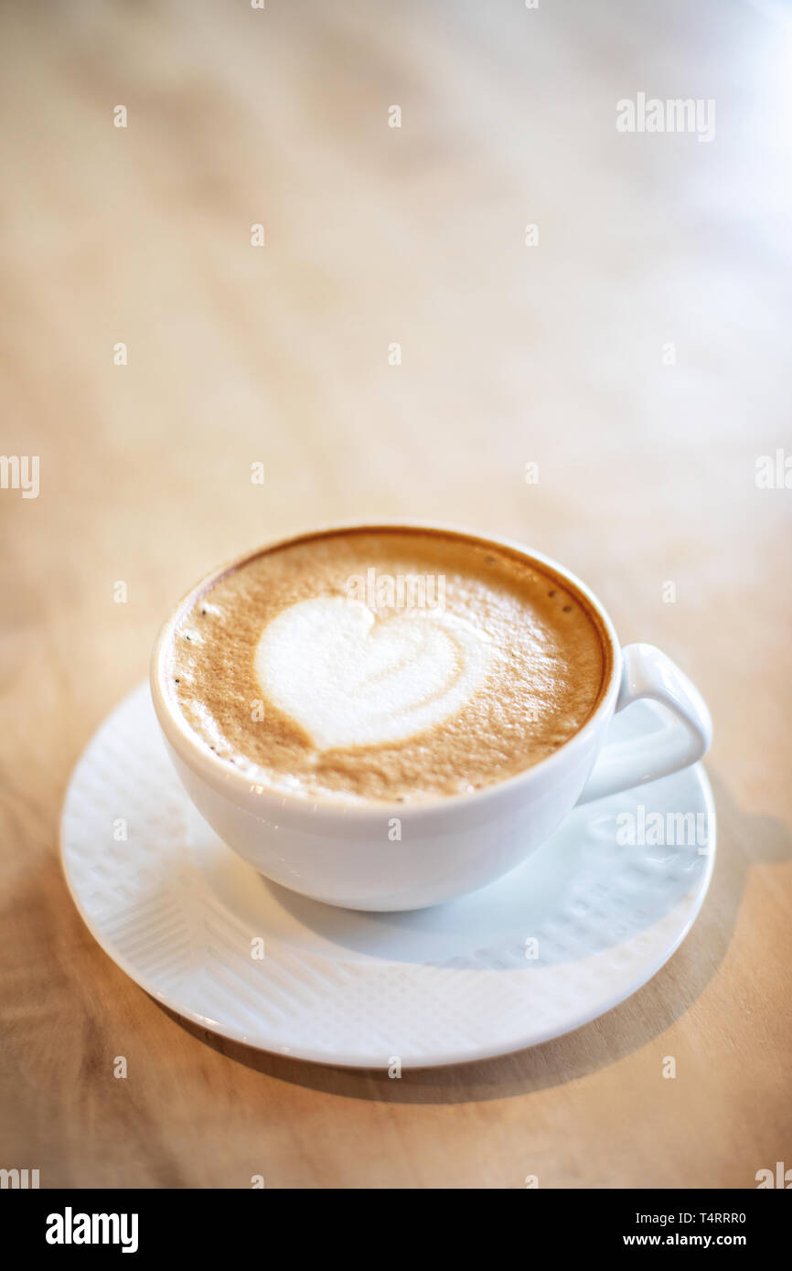 White cappuccino cup with with latte art heart placed on light brown ...