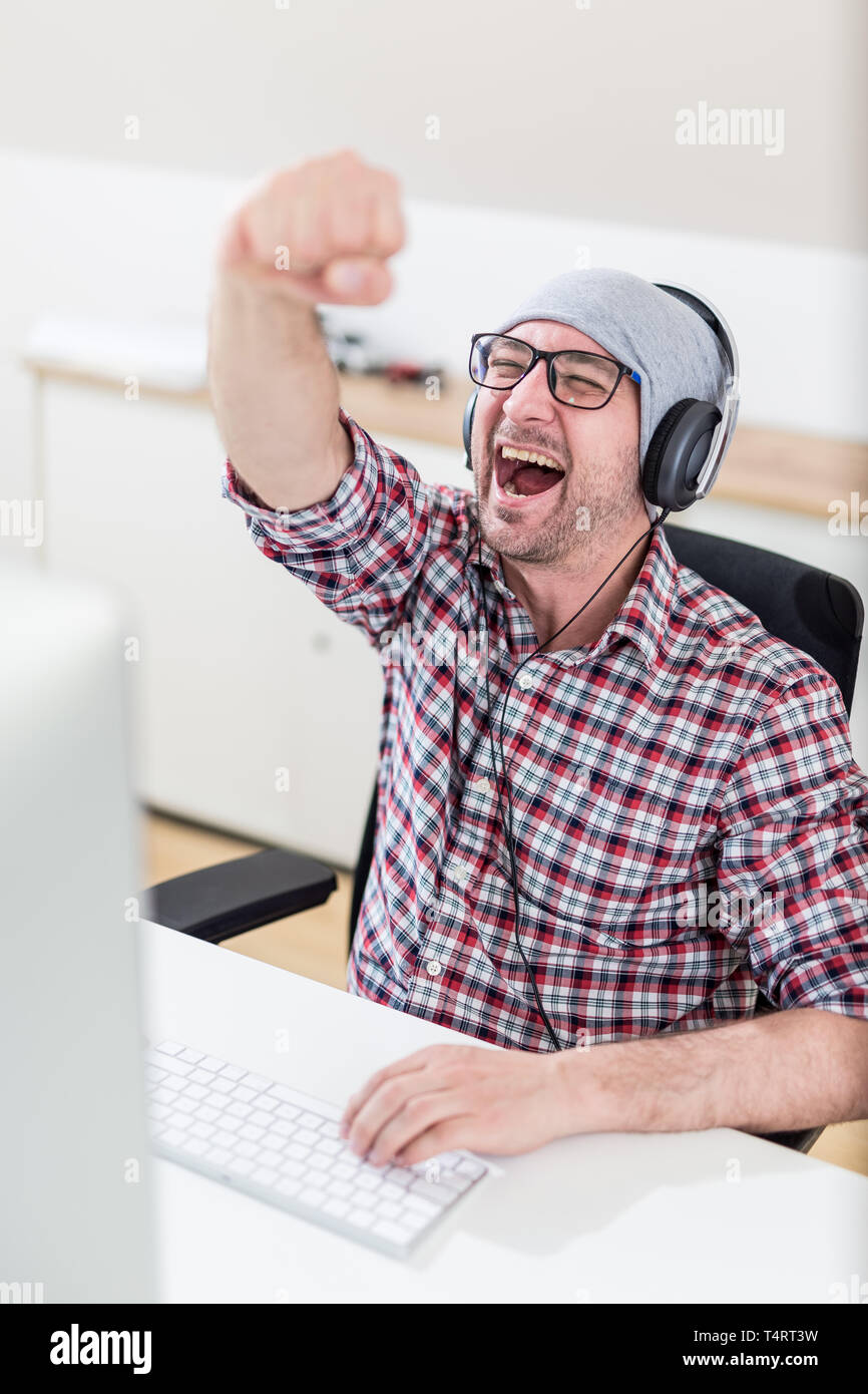 Cheerful modern man with headphones sitting at the desk and working on ...