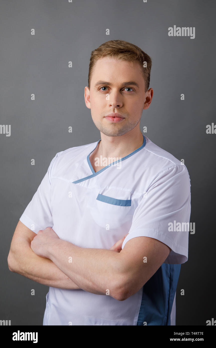 Young sympathetic doctor stands isolated on a grey background dressed ...