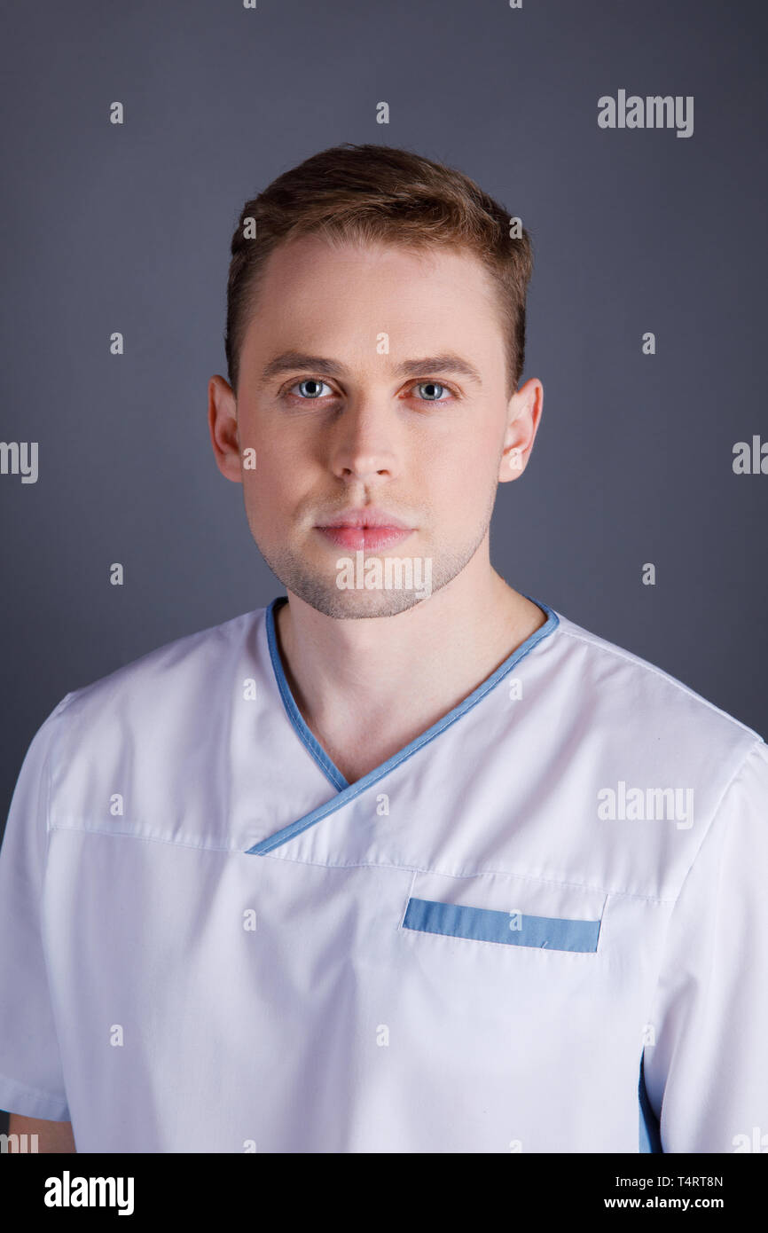 Young sympathetic doctor stands isolated on a grey background dressed ...