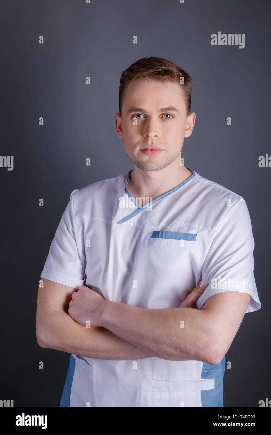 Young sympathetic doctor stands isolated on a grey background dressed ...