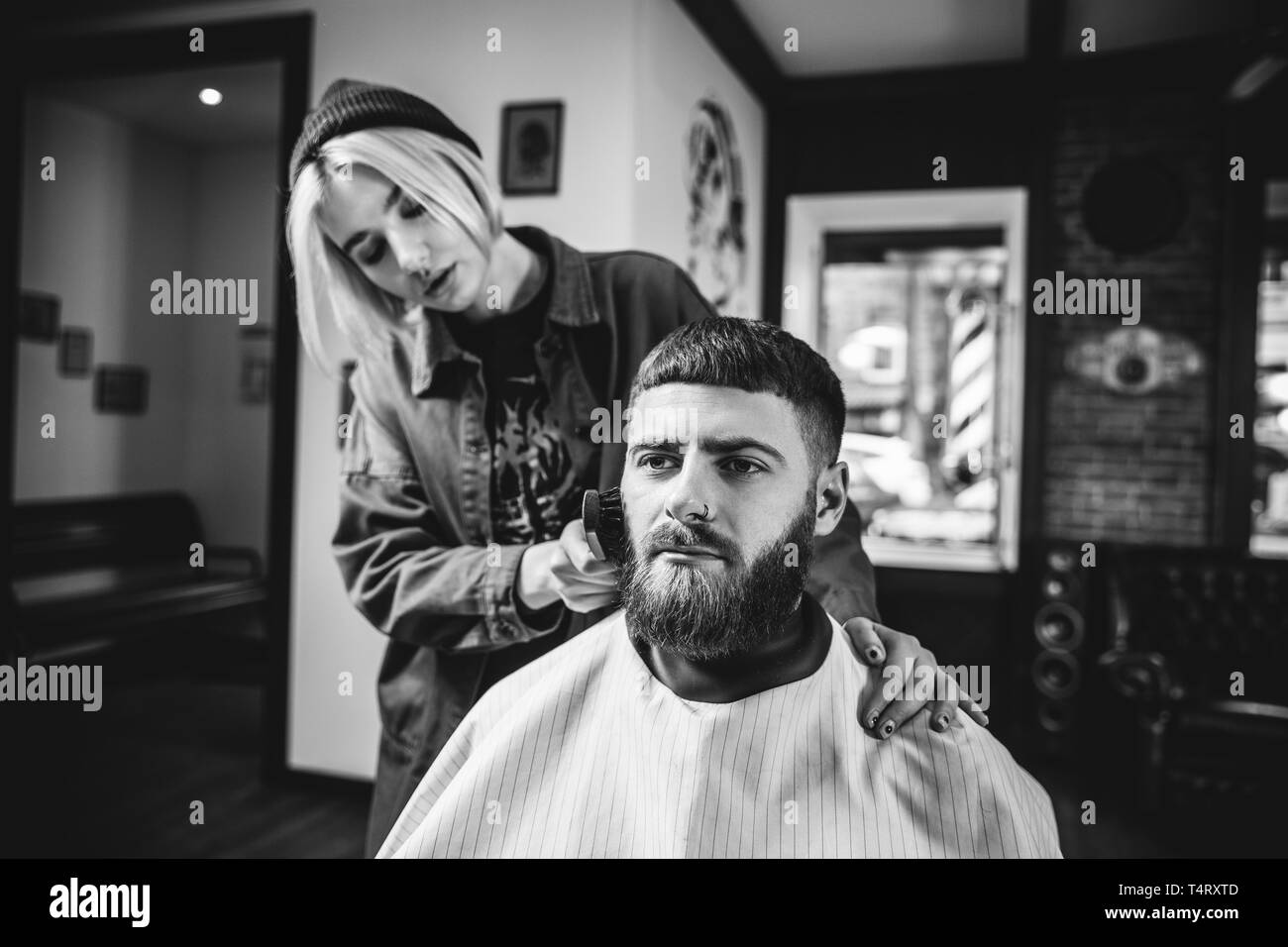 Young woman making haircut for bearded man at barbershop. Female barber ...