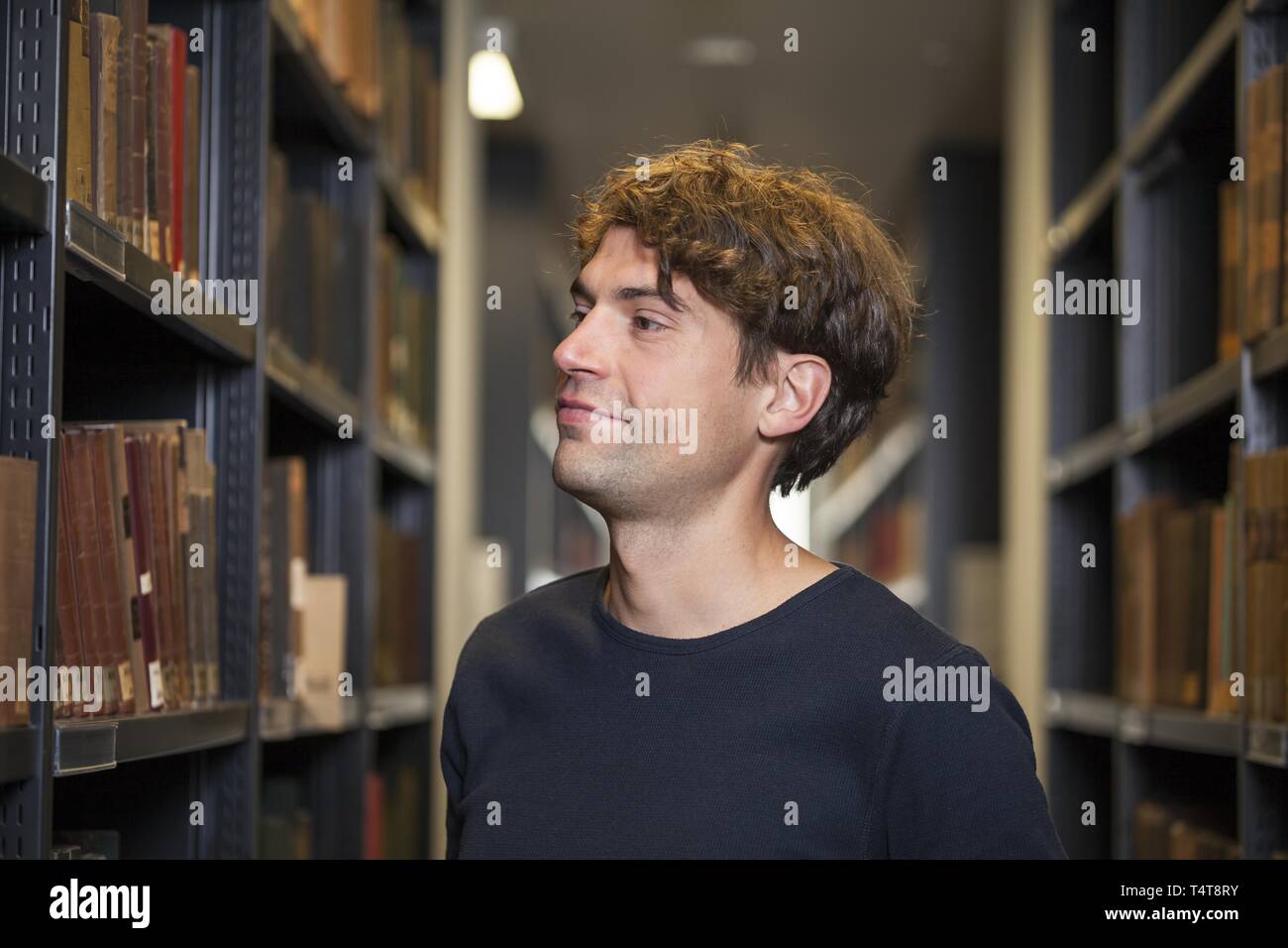 Student at bookshelf in library Stock Photo - Alamy