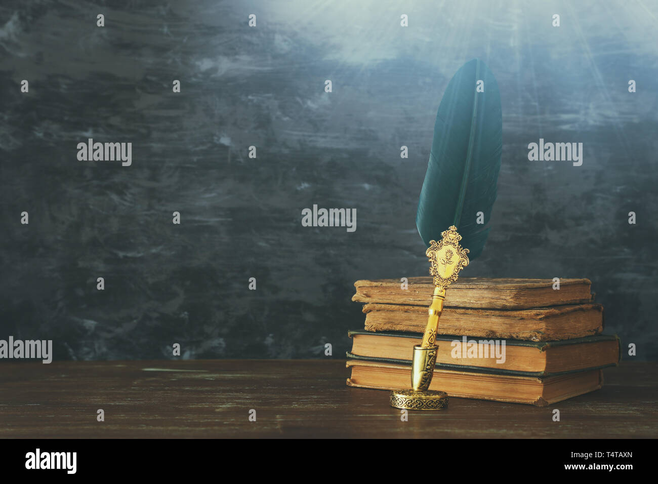 Old feather quill ink pen with inkwell and old books over wooden desk ...