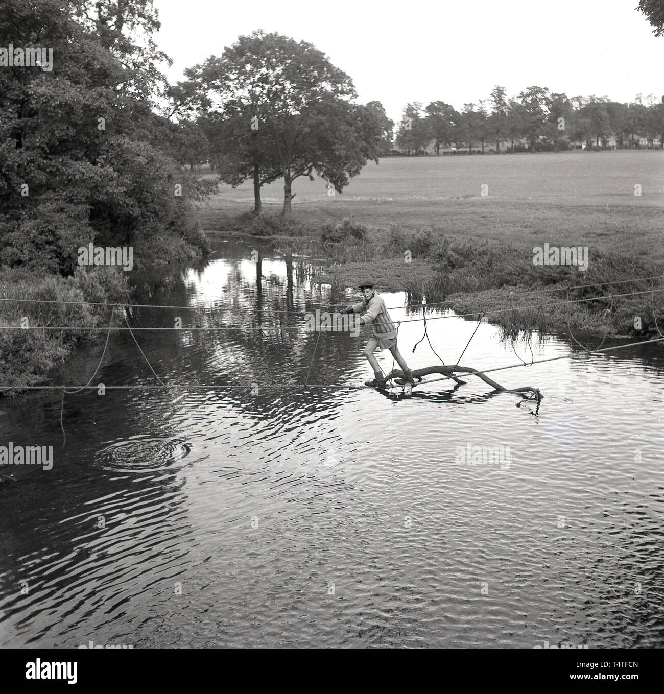 1960s, historical, a young adventure scout crosses a river on a rope ...