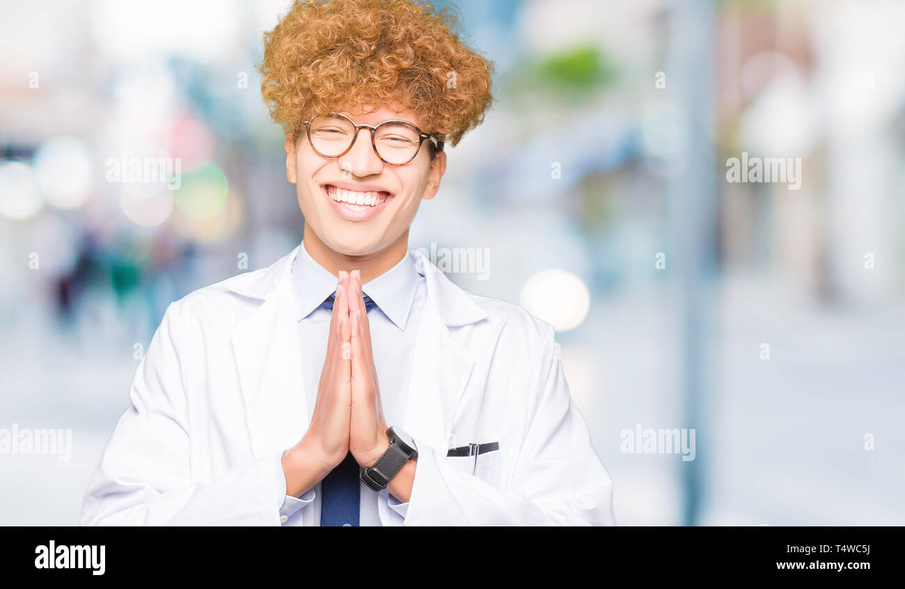 Young handsome scientist man wearing glasses praying with hands ...