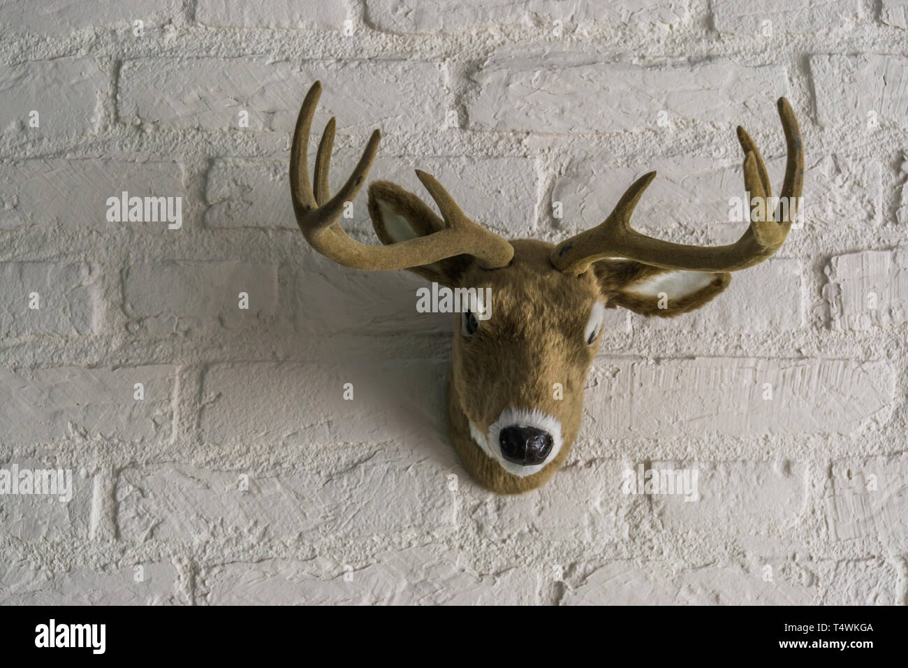 artificial male deer head with antlers hanging on a white brick wall ...