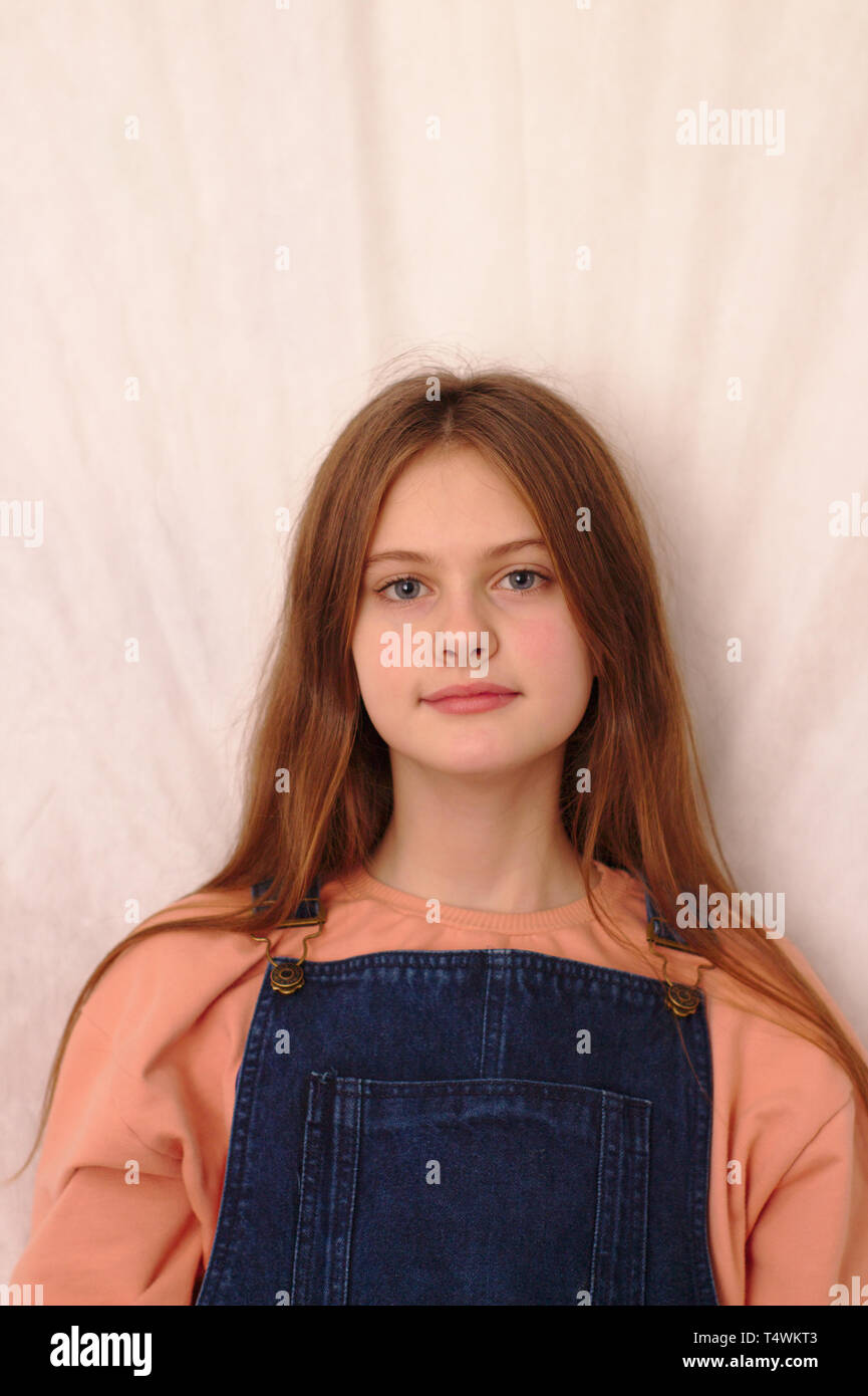 blue eyed brown haired shy girl in denim overalls. Studio model shot ...