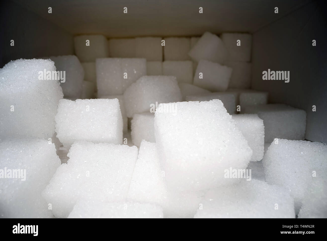 Macro shot of sugar cubes next to carton box on wooden table. Unhealthy ...