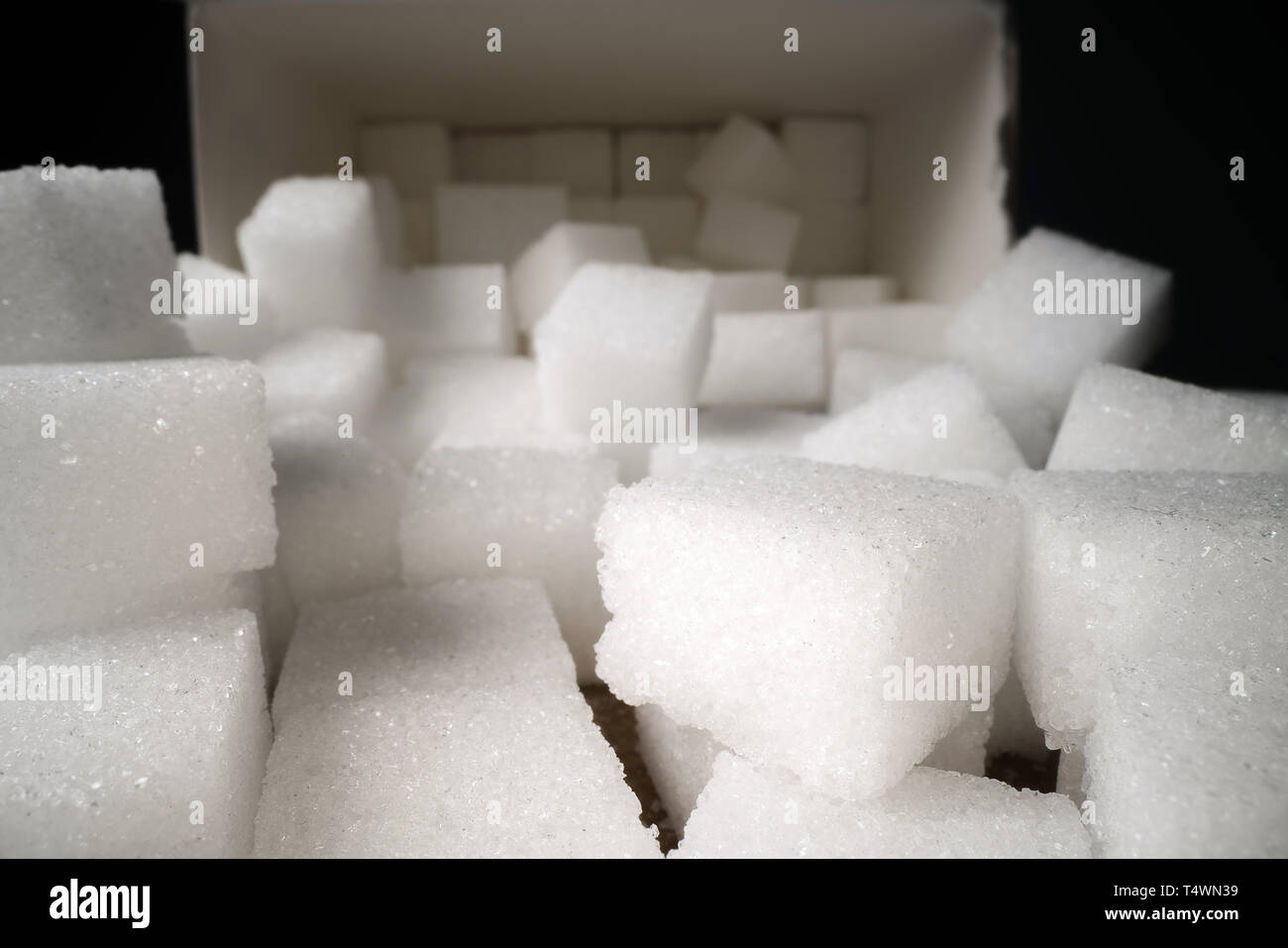 Macro shot of sugar cubes next to carton box on wooden table. Unhealthy ...